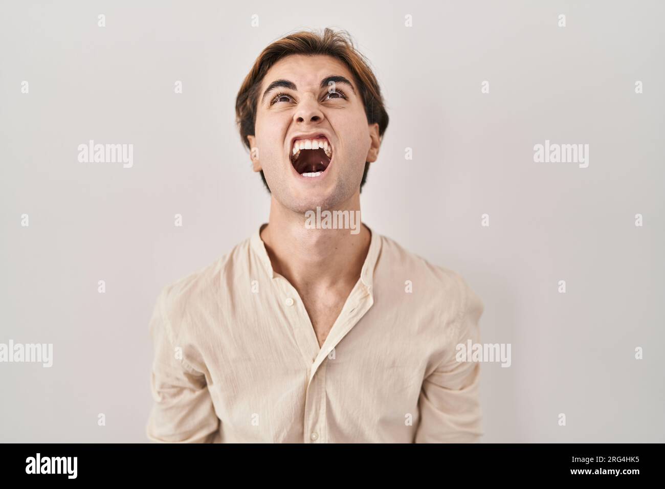 Young man standing over isolated background angry and mad screaming ...