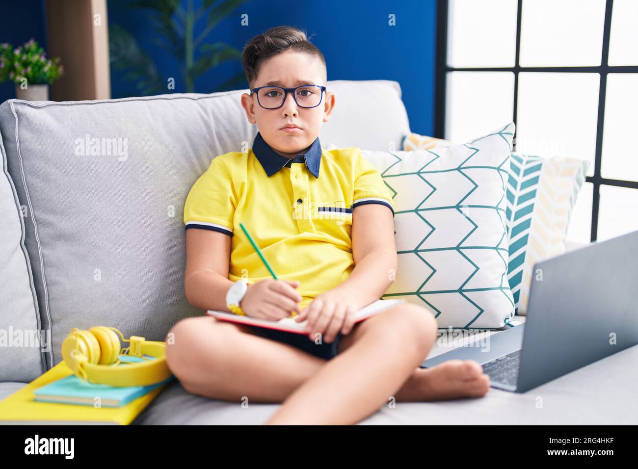 Young hispanic kid doing homework sitting on the sofa depressed and ...