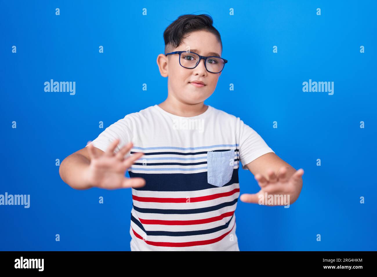 Young hispanic kid standing over blue background afraid and terrified ...