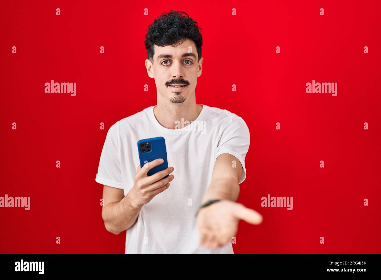 Hispanic man using smartphone over red background smiling cheerful ...