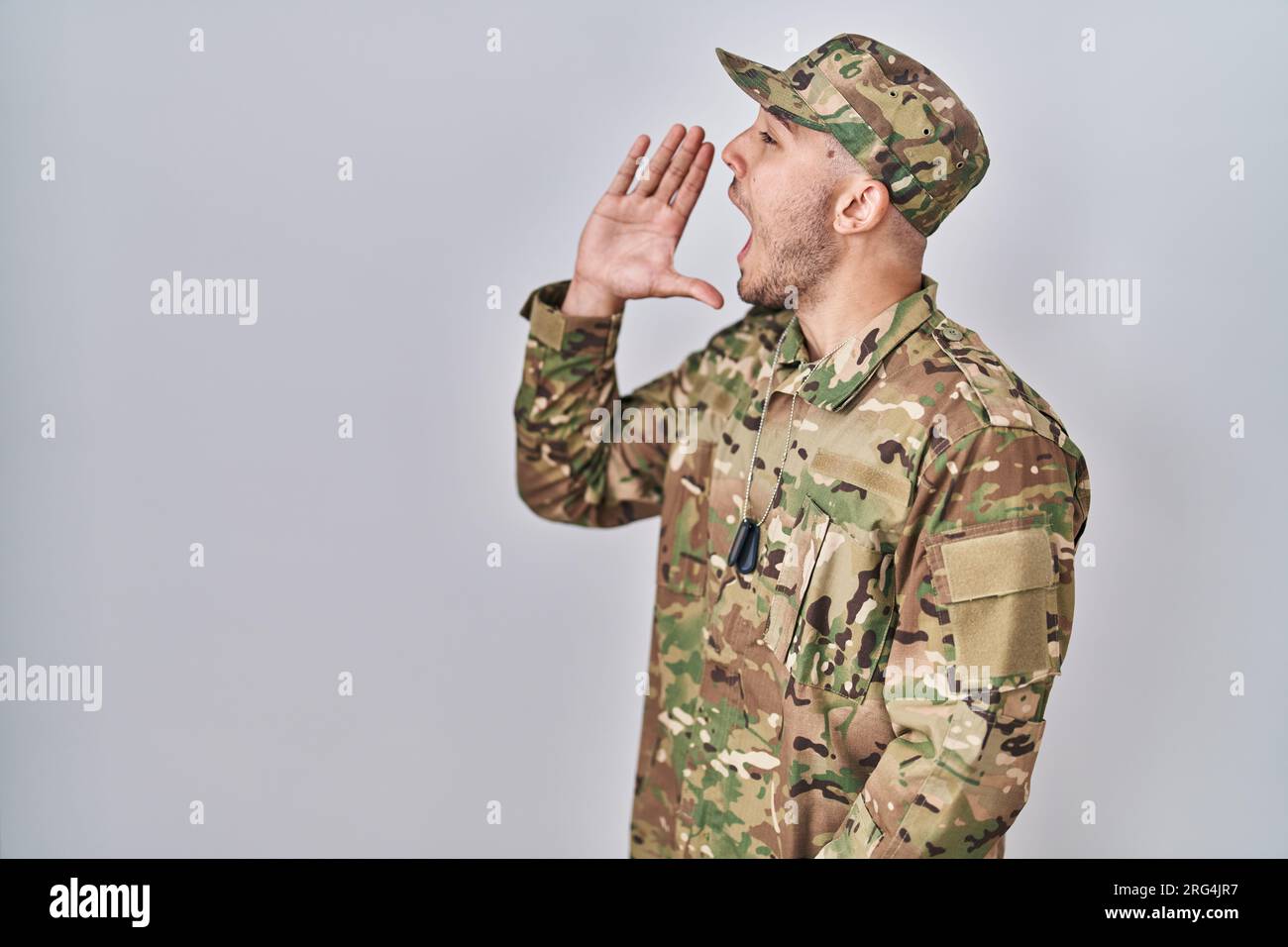 Young hispanic man wearing camouflage army uniform shouting and ...