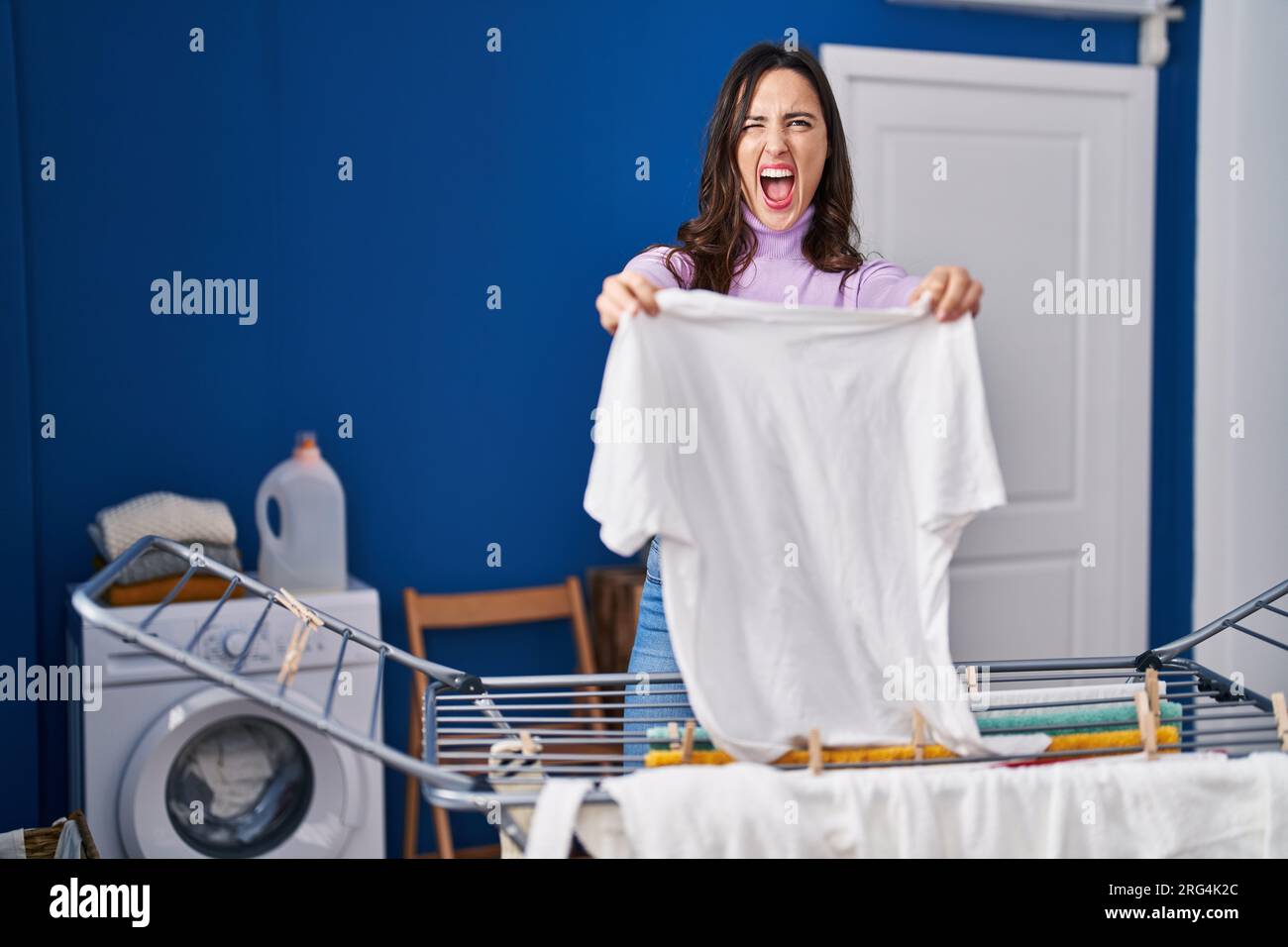 Young brunette woman hanging clothes at clothesline angry and mad ...