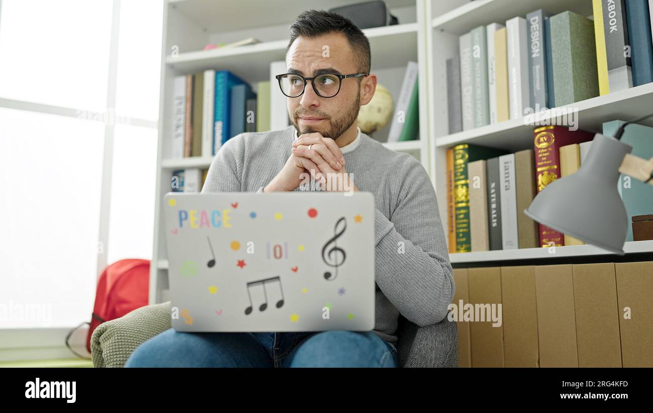 Hispanic man using laptop thinking sitting on a chair at library ...