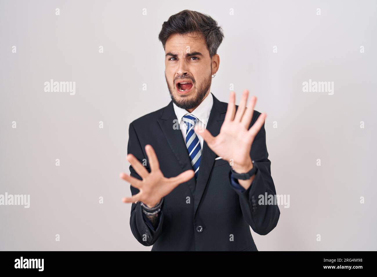Young hispanic man with tattoos wearing business suit and tie afraid ...