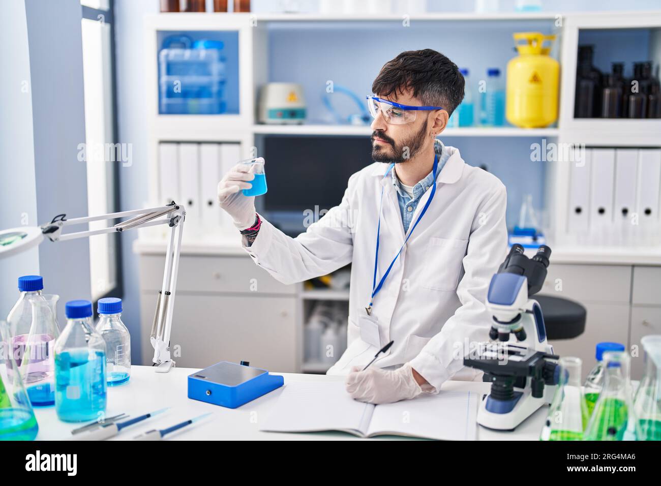 Young hispanic man scientist writing on notebook measuring liquid at ...