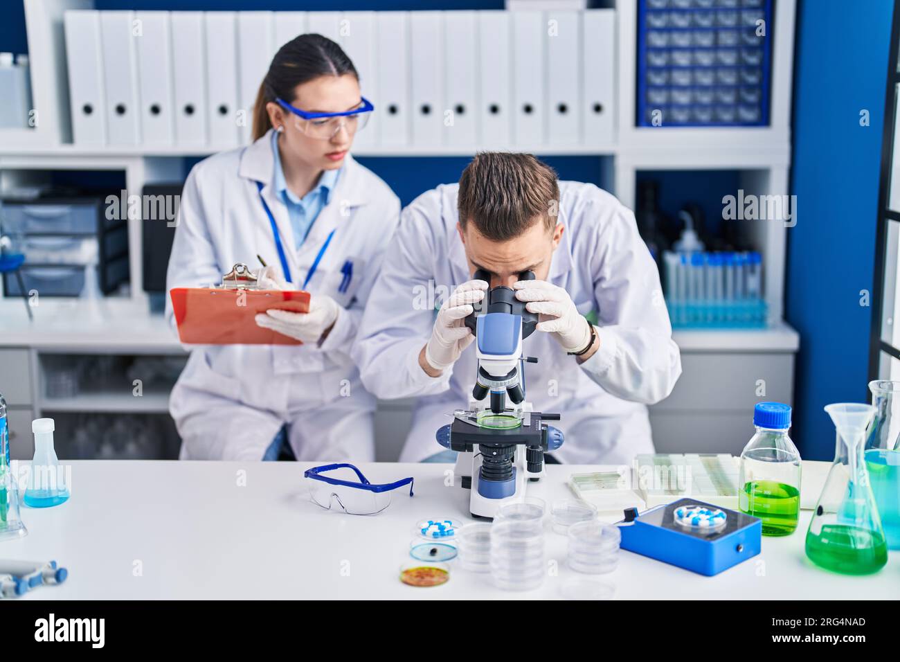 Man and woman scientists using microscope write on clipboard at ...