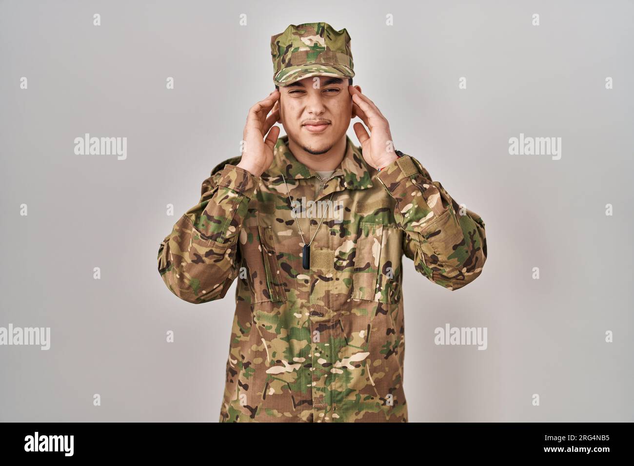 Young arab man wearing camouflage army uniform covering ears with ...
