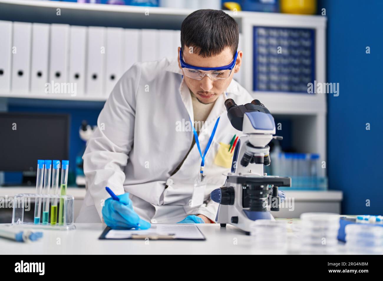 Young man scientist writing on document using mircoscope at laboratory ...