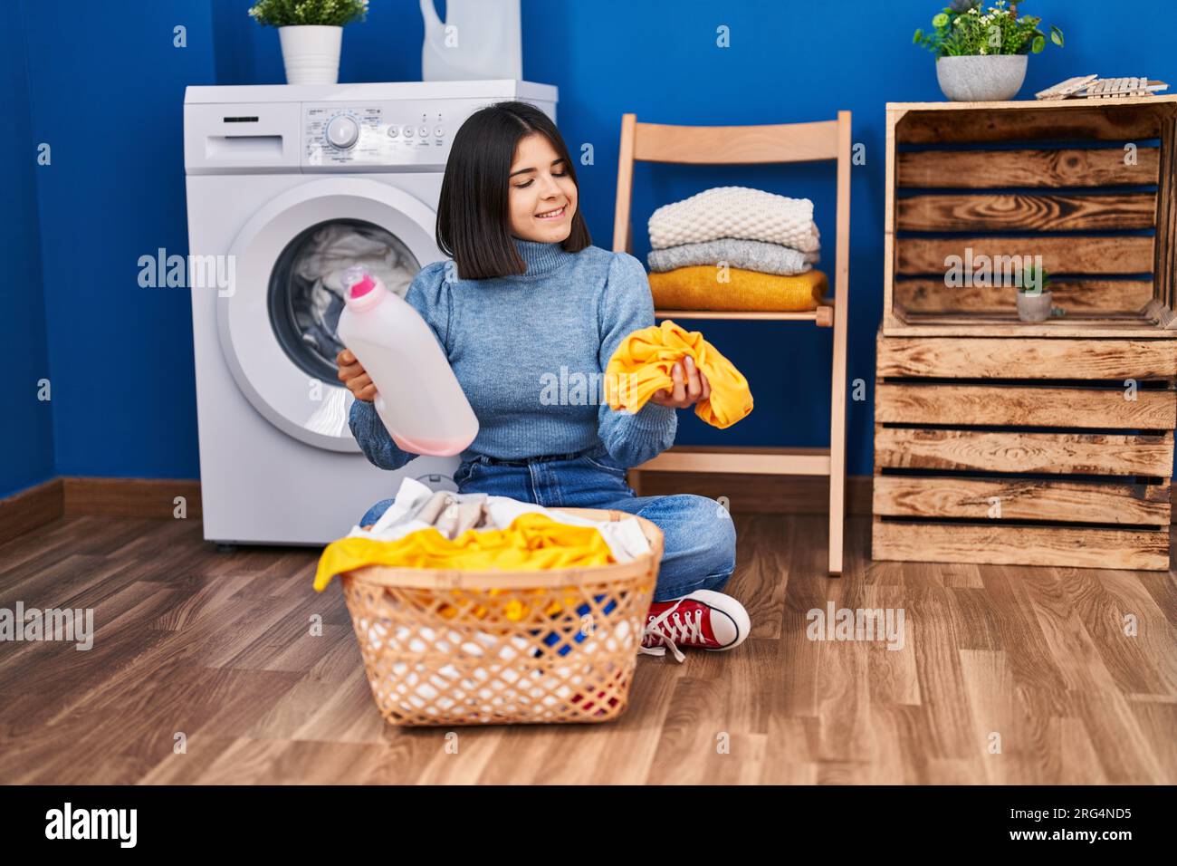 Young beautiful hispanic woman washing clothes holding detergent bottle ...