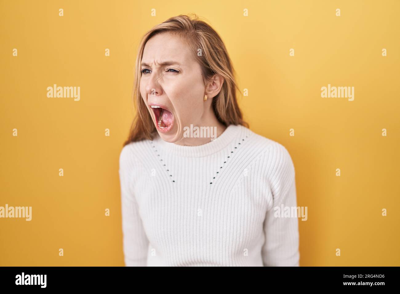 Young caucasian woman wearing white sweater over yellow background ...