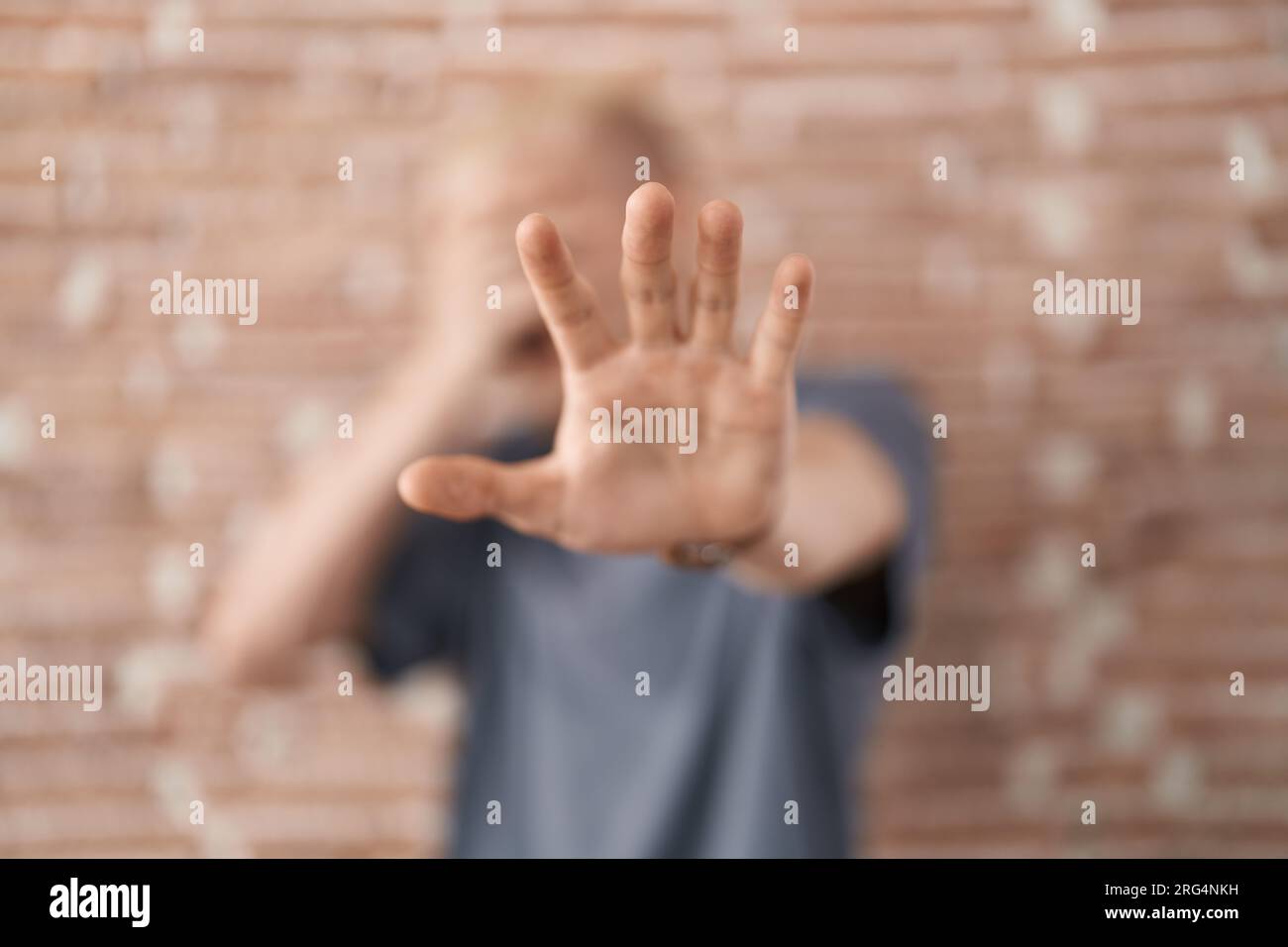 Young caucasian man standing over bricks wall covering eyes with hands ...
