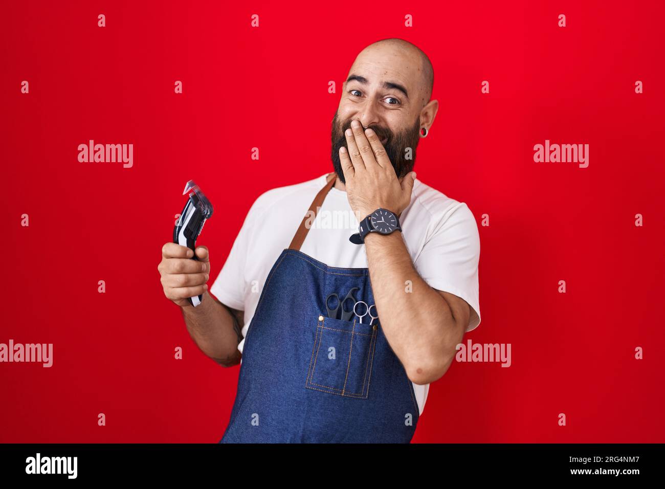 Young hispanic man with beard and tattoos wearing barber apron holding ...