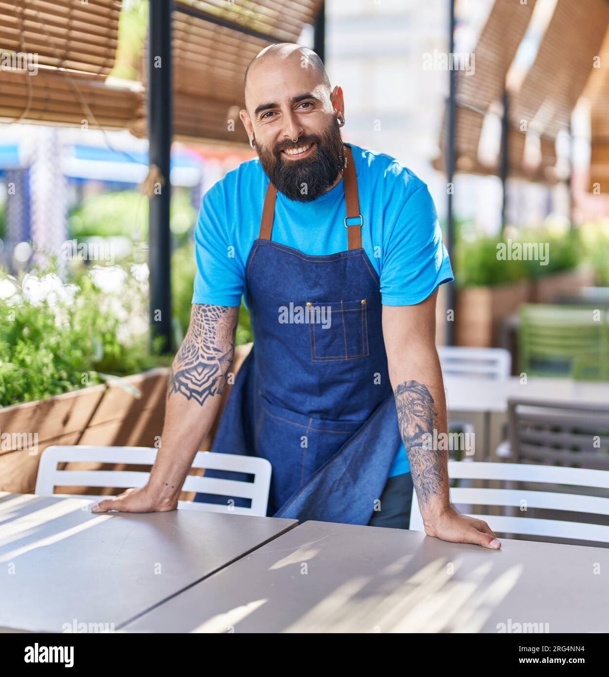 Young bald man waiter smiling confident standing at coffee shop terrace ...