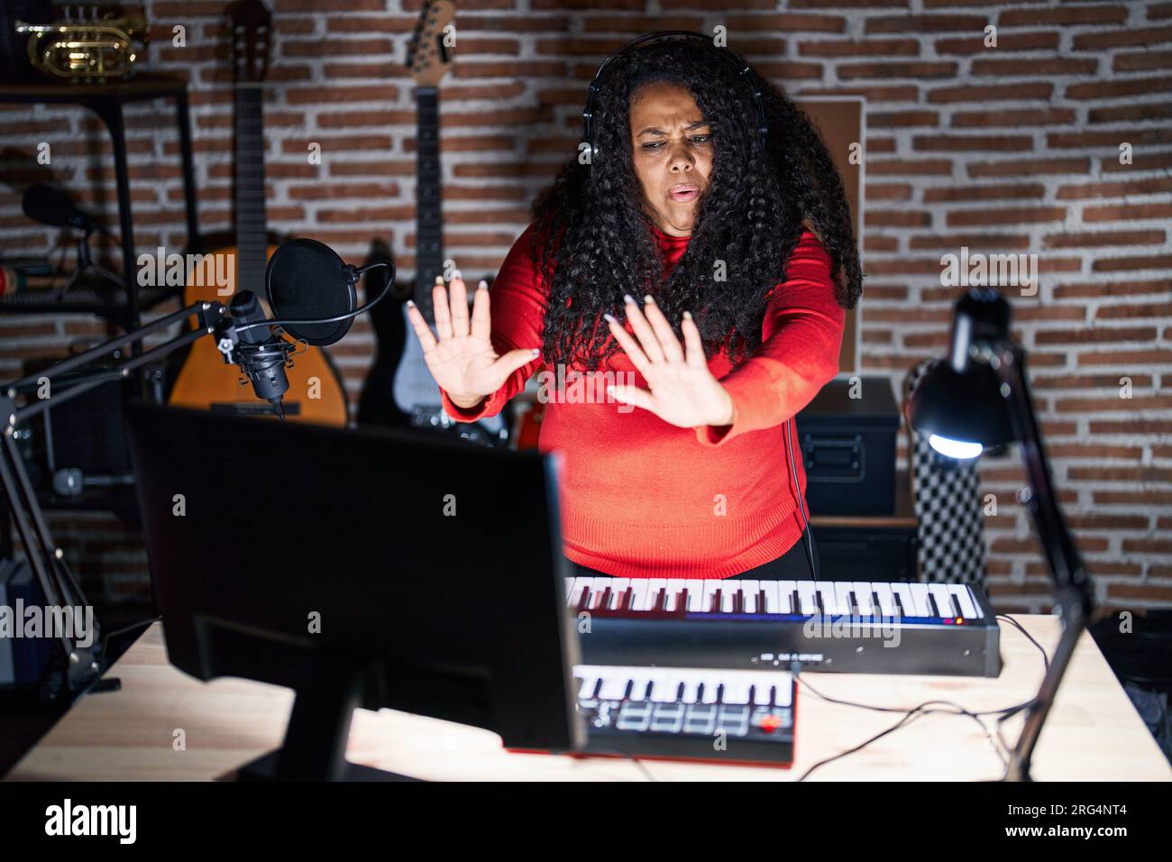 Plus size hispanic woman playing piano at music studio afraid and ...