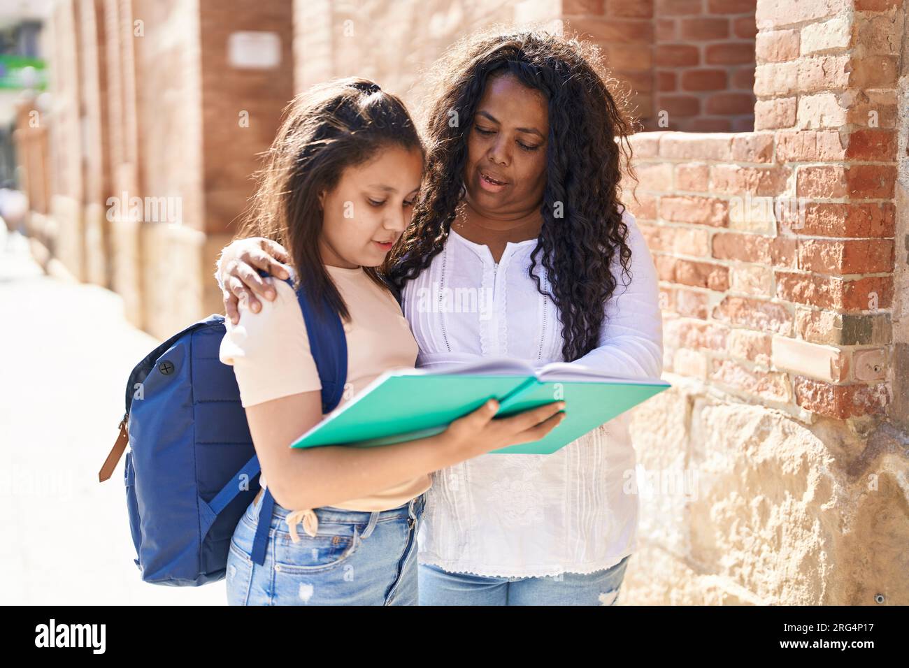 Mother and daughter reading book hugging each other at street Stock ...