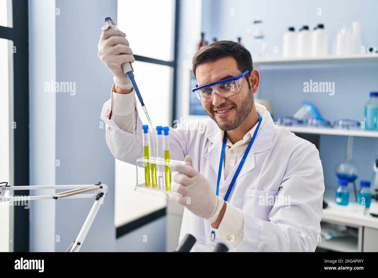 Young hispanic man scientist measuring liquid using pipette at ...
