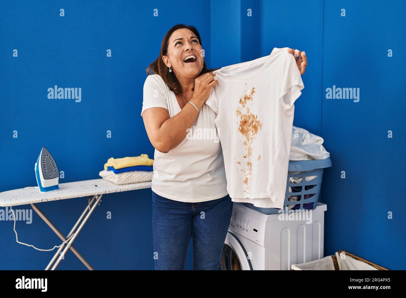 Middle age hispanic woman putting dirty laundry into washing machine ...