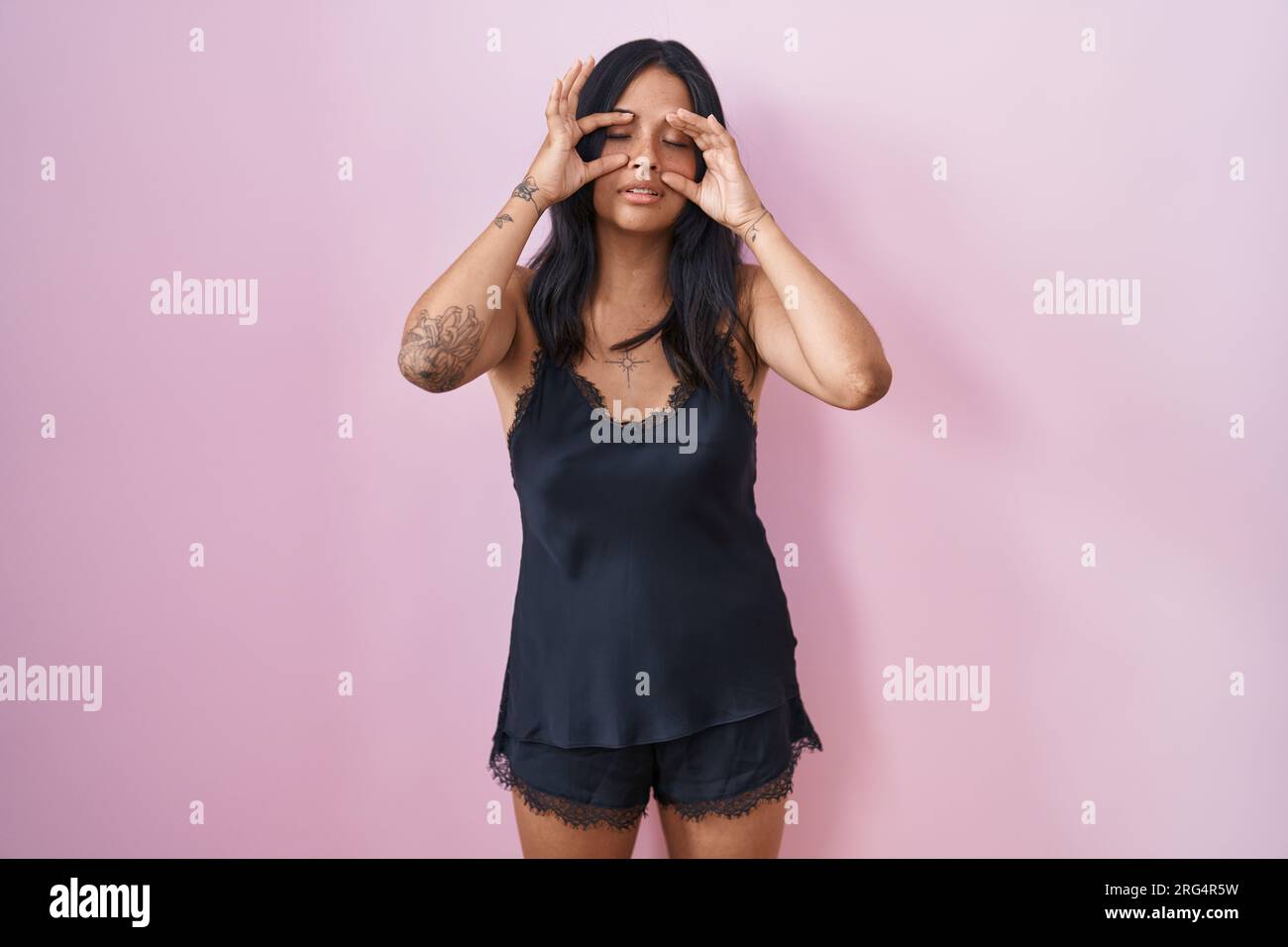 Brunette woman wearing black pajama trying to open eyes with fingers ...