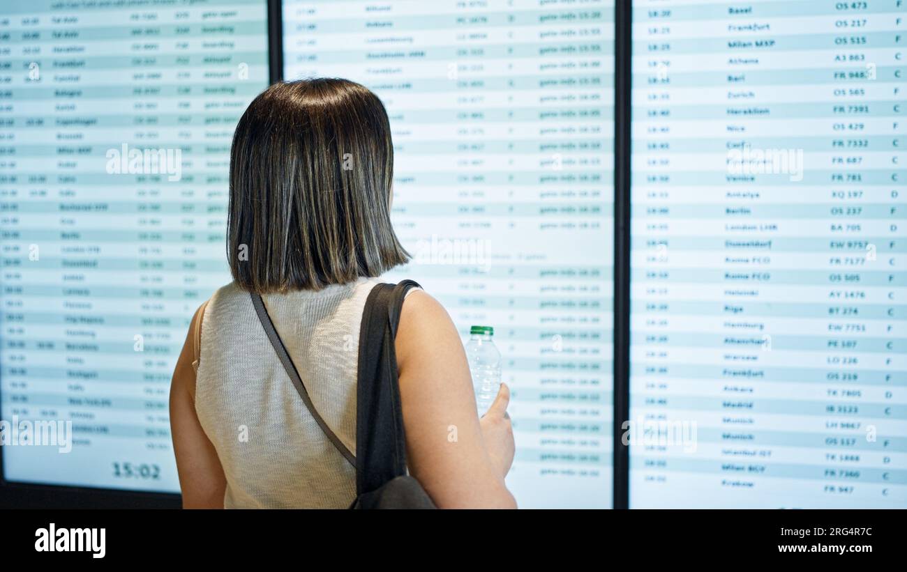 Young beautiful hispanic woman looking at flight destination display at ...