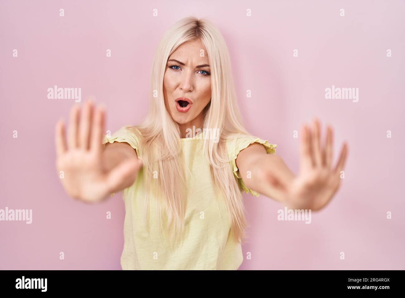 Caucasian woman standing over pink background doing stop gesture with ...