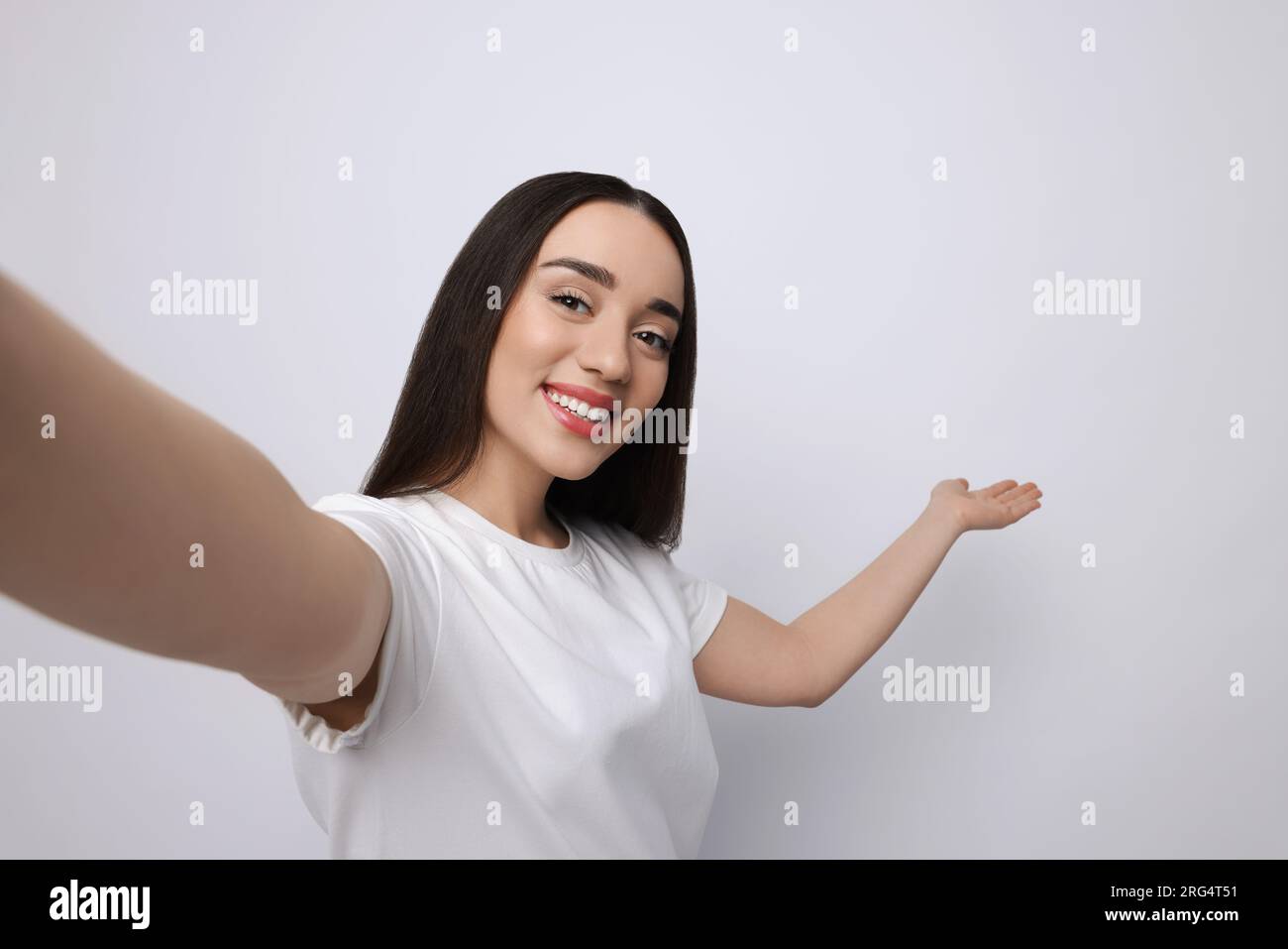 Smiling young woman taking selfie on white background, space for text ...