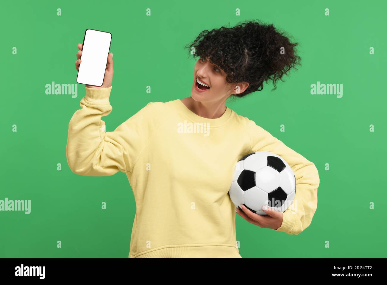 Happy fan holding soccer ball and showing smartphone on green ...