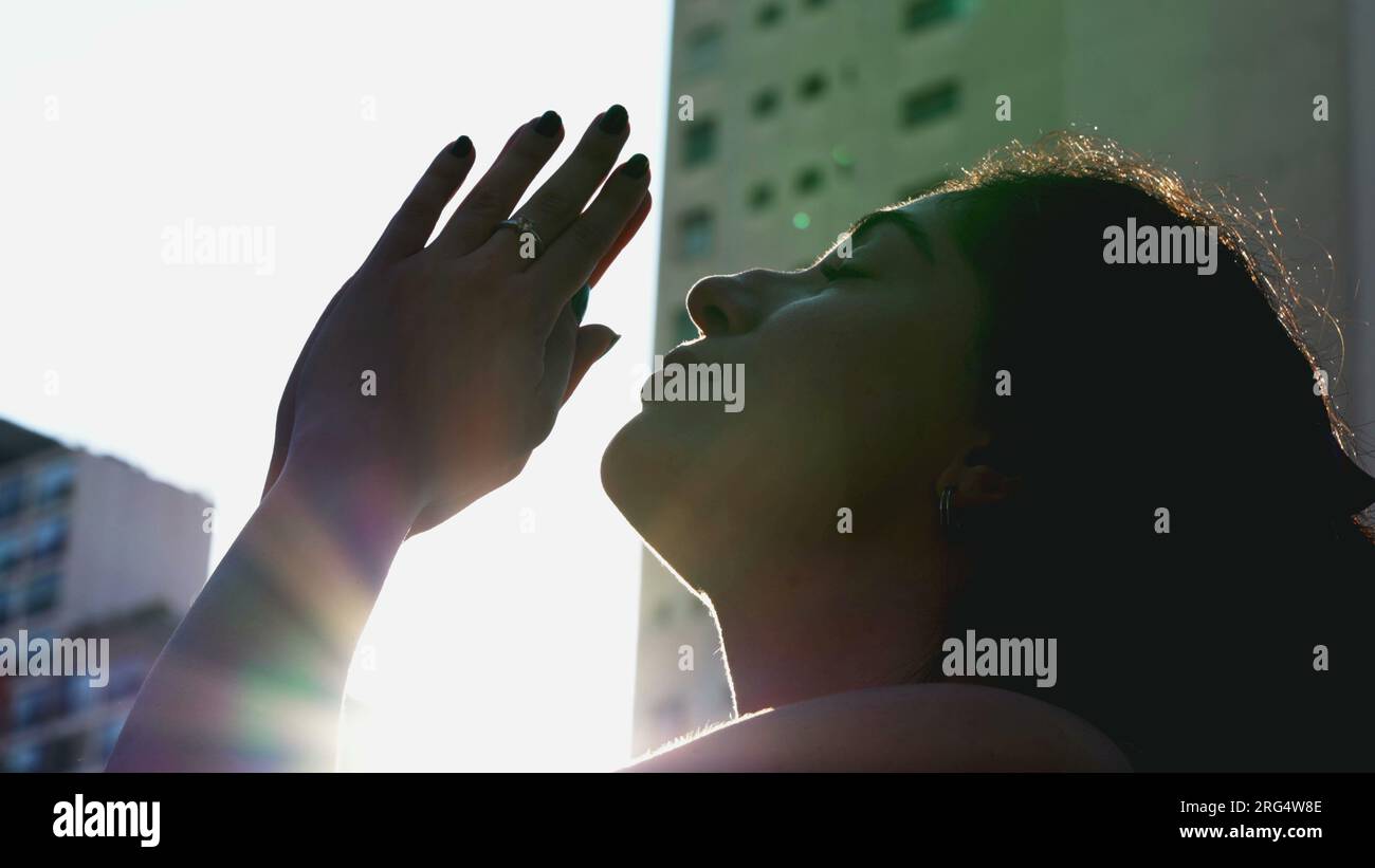 Peaceful young woman praying outside in the sunlight. Spiritual person ...