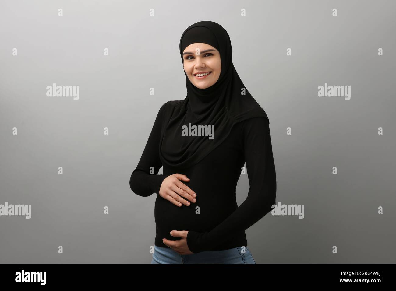 Portrait of pregnant Muslim woman in hijab on light gray background ...