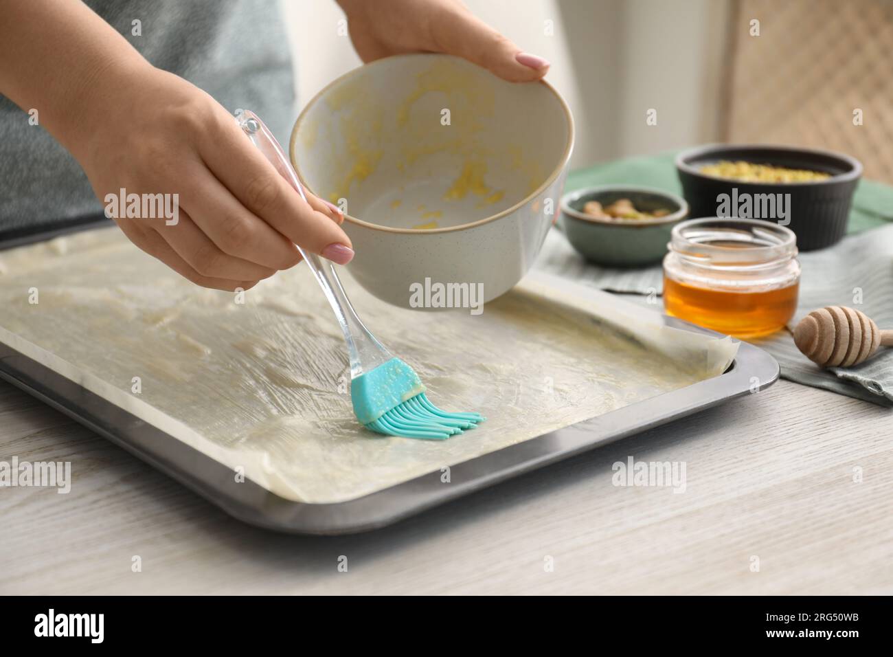 Making delicious baklava. Woman buttering dough in baking pan at white ...