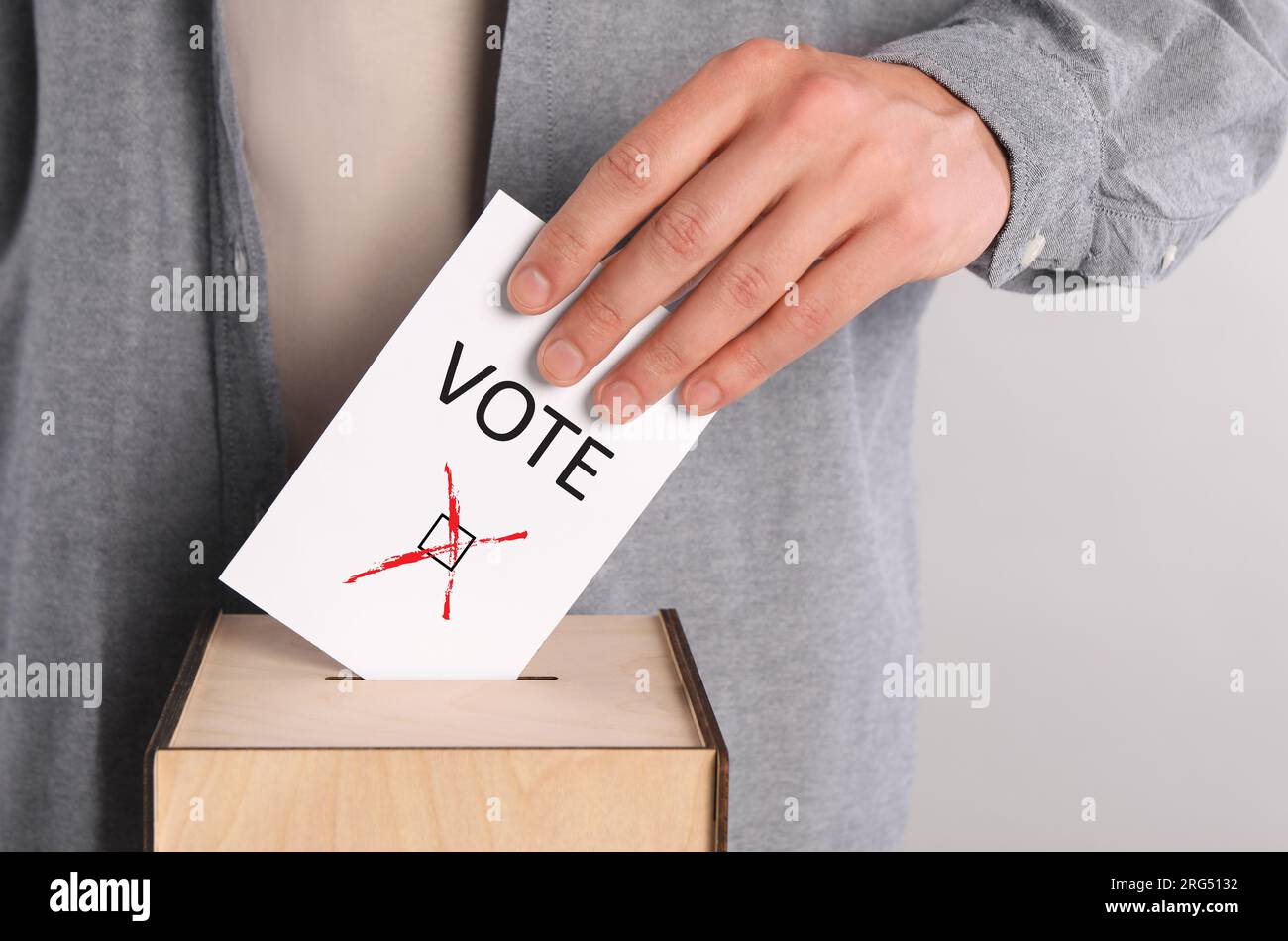 Man putting paper with word Vote and tick into ballot box on light grey ...