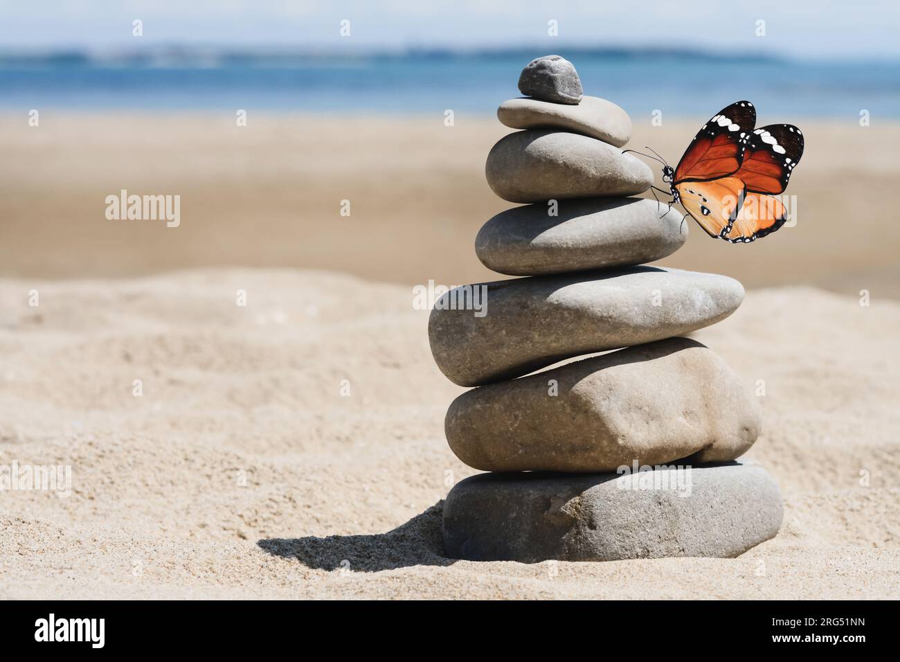 Peace and harmony. Stacked pebbles on sand and beautiful butterfly near ...