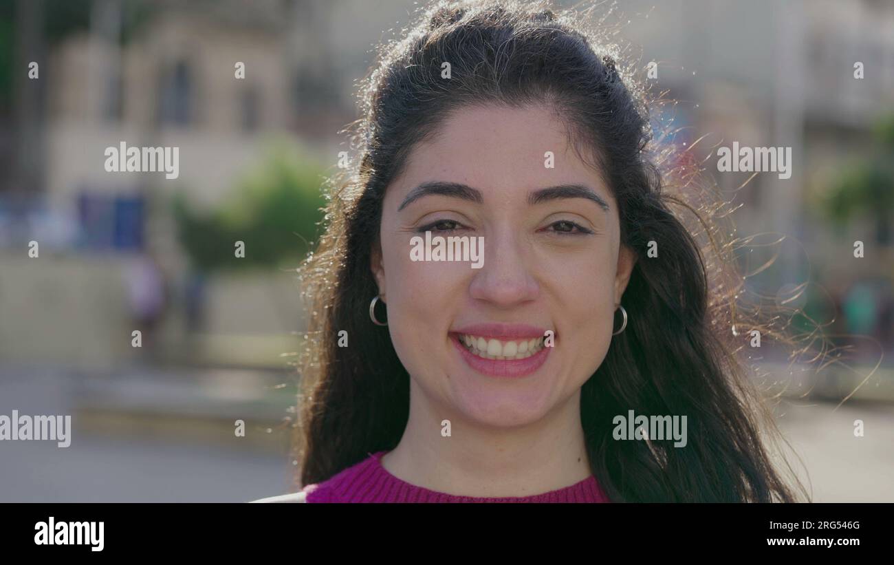 Portrait of a happy young woman smiling outside standing in city park ...