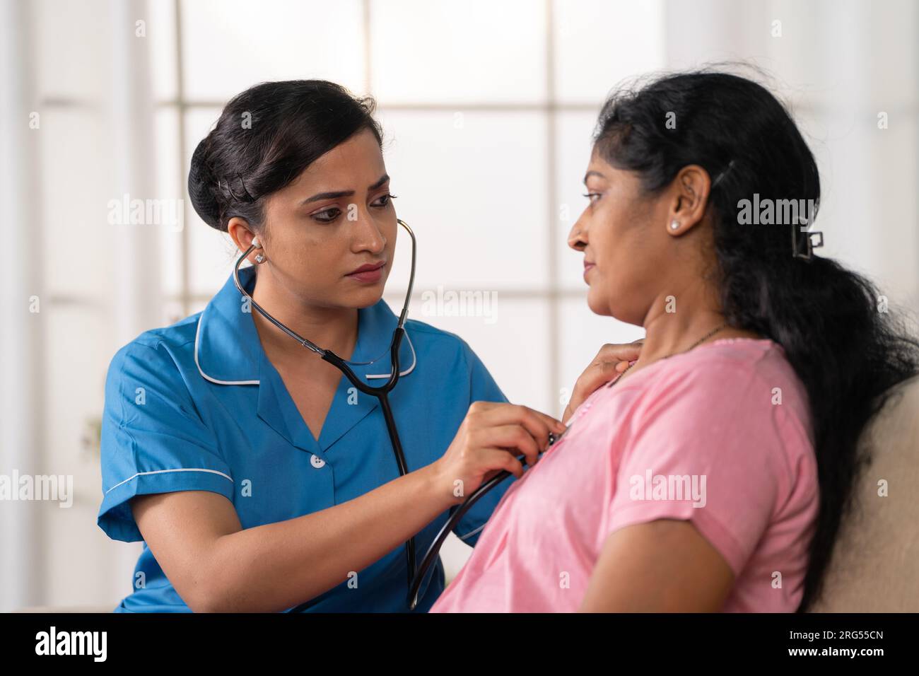 Indian nurse or doctor examining sick woman patient using stethoscope on sofa at home - concept ...