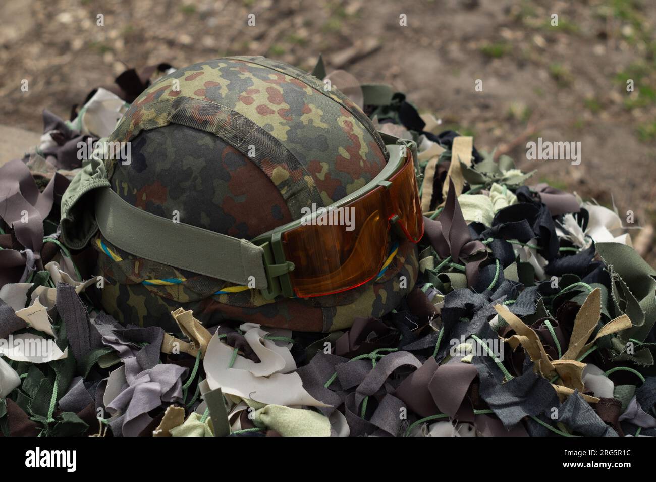 Military helmet with tactical goggles lies on a camouflage net ...