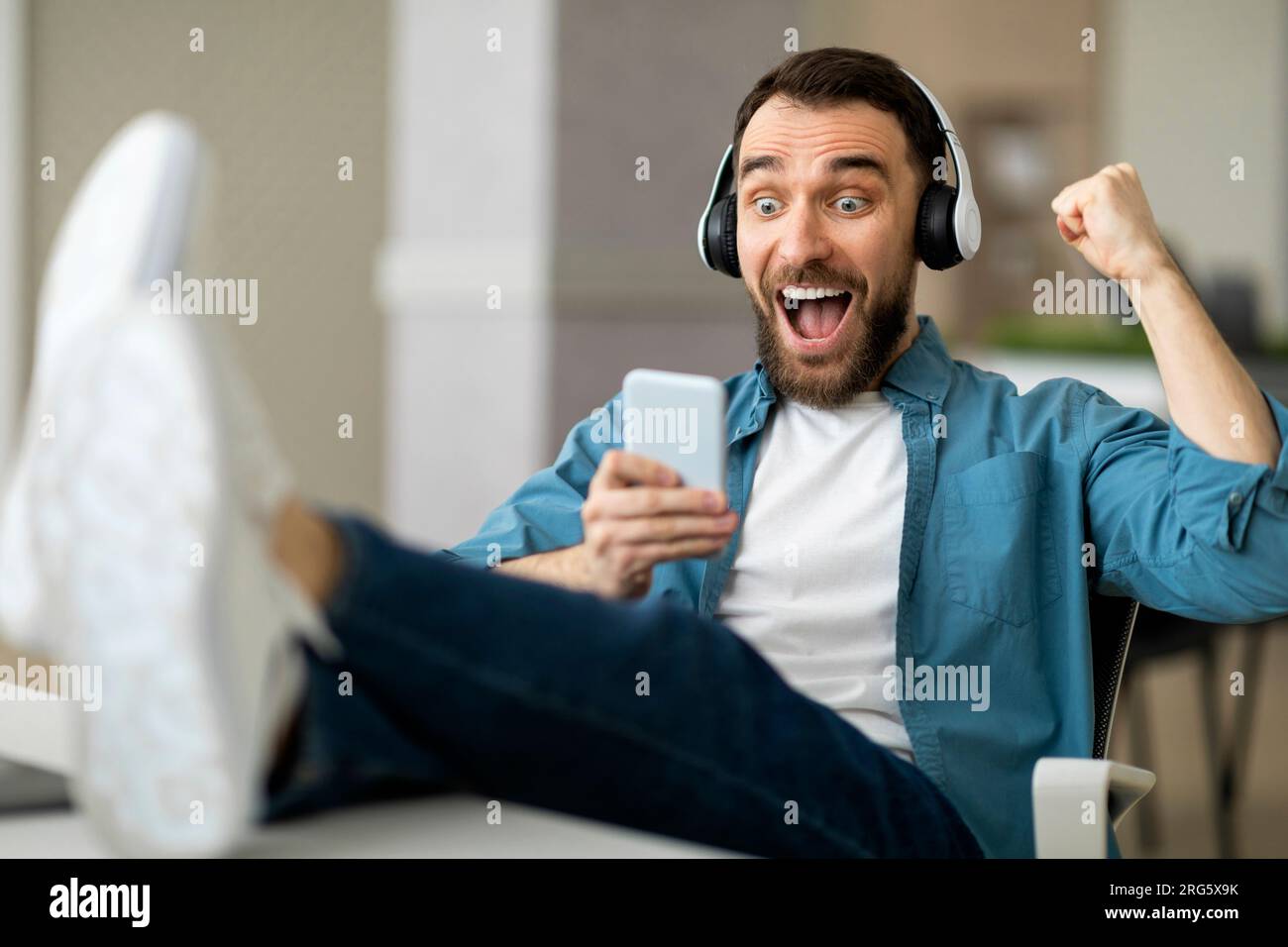 Excited Young Man In Headphones Holding Smartphone And Shouting Yes ...