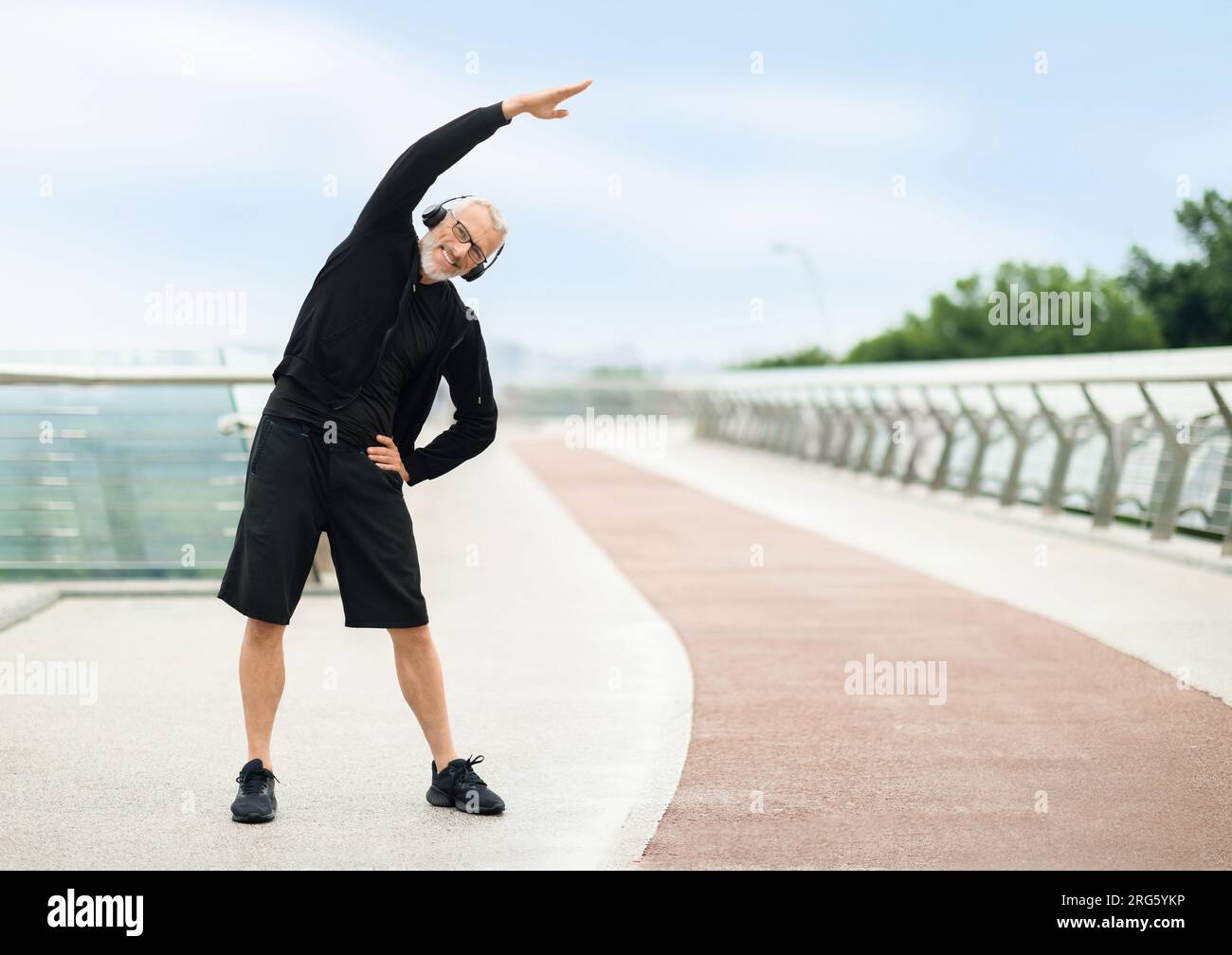 Athletic elderly sportsman stretching body while exercising outdoor ...