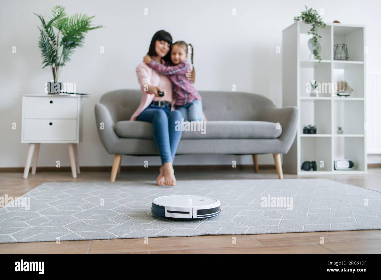 Mom Hugging Kid And Turning On Cleaning Robot In Living Room Stock