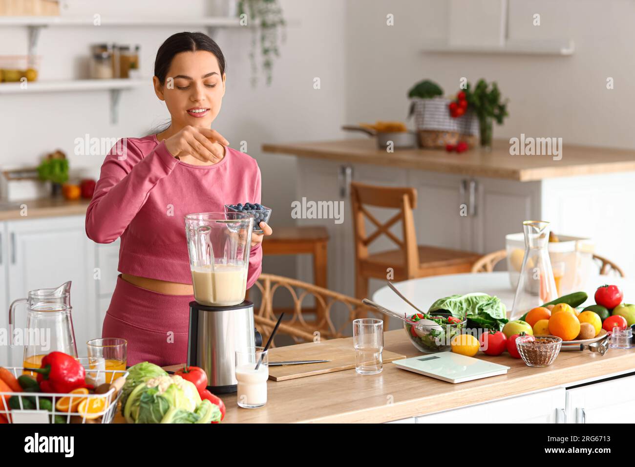 Sporty young woman making healthy smoothie with blueberries in kitchen ...