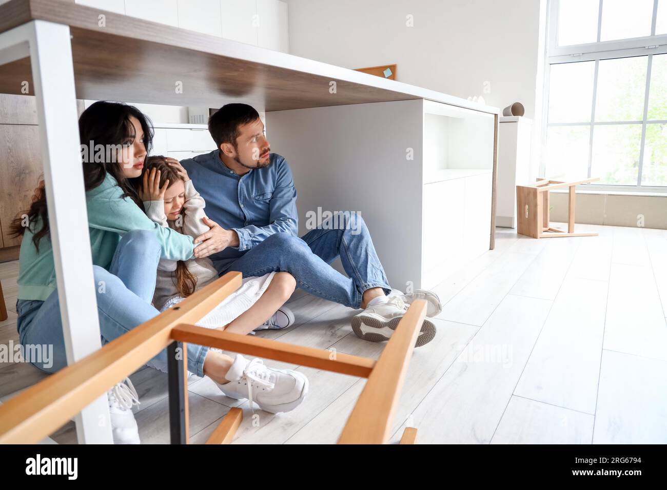 Scared family hiding under dining table during earthquake in kitchen ...