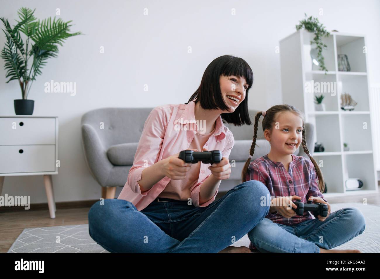 Portrait of cheerful mother and cute daughter sitting cross-legged with ...