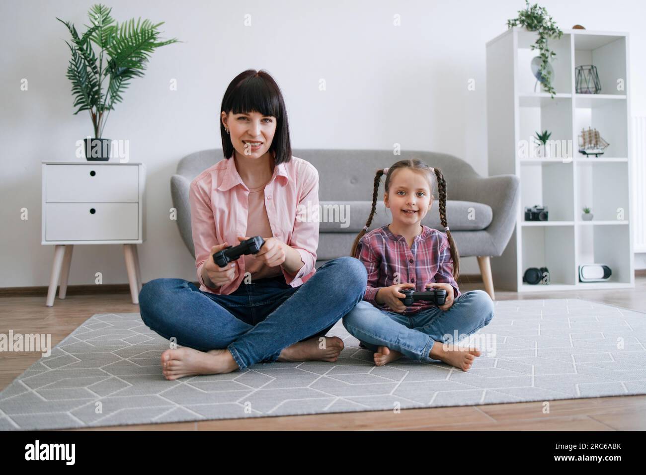 Portrait of cheerful mother and cute daughter sitting cross-legged with ...