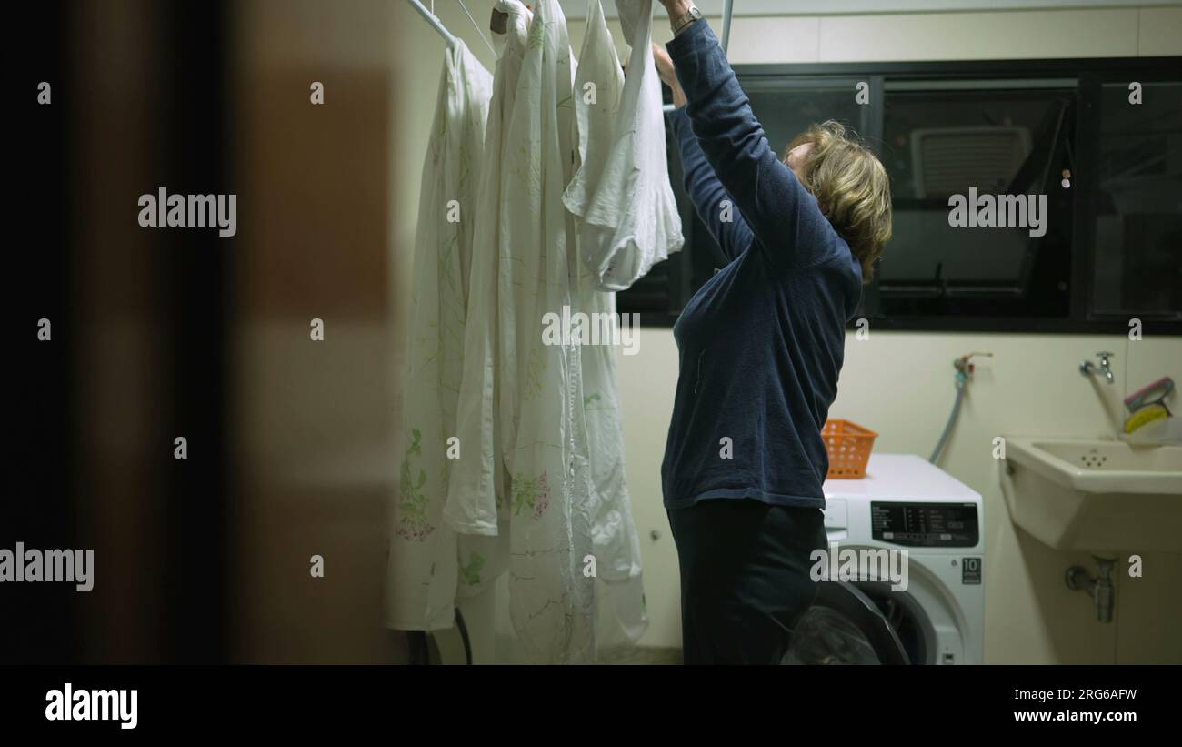 Candid older lady putting clothes to dry on laundry rack. Real life ...