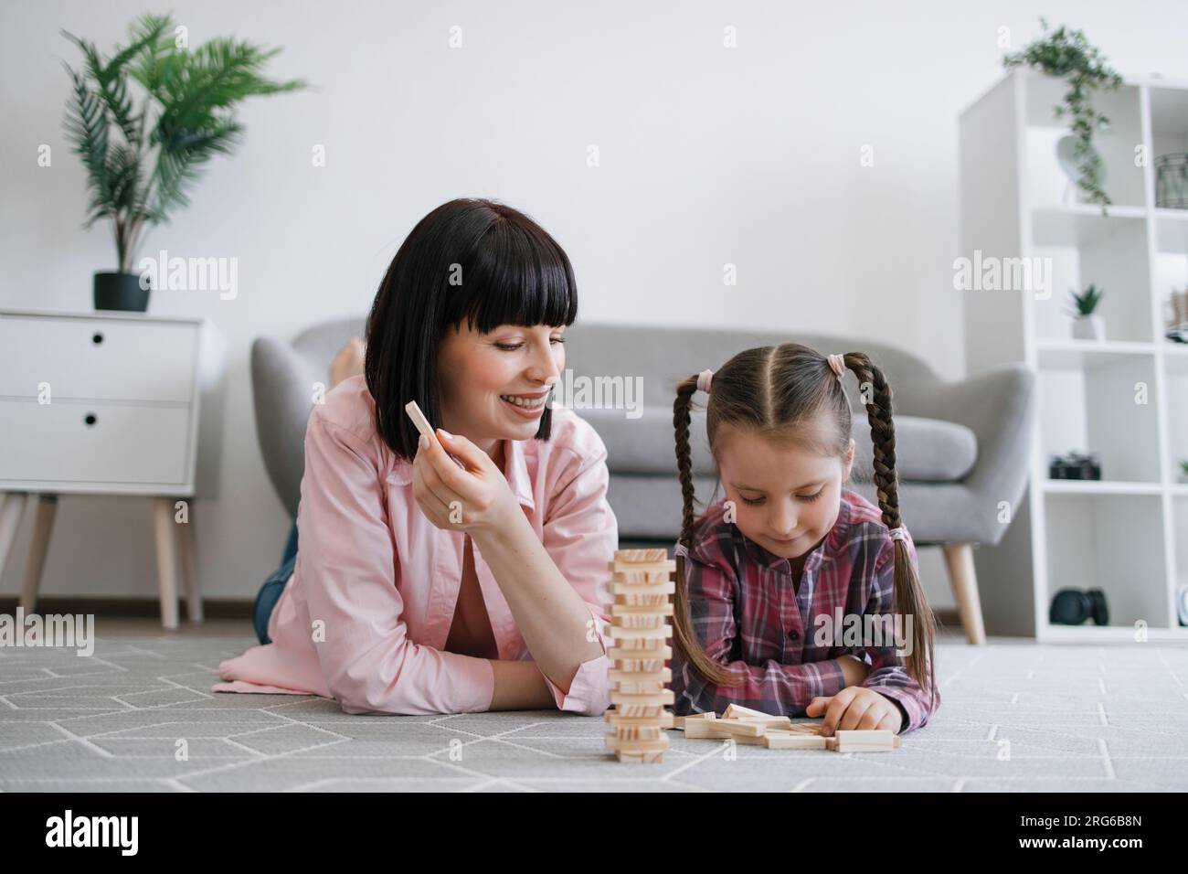 Child putting blocks in tumble tower while mom lying aside Stock Photo ...