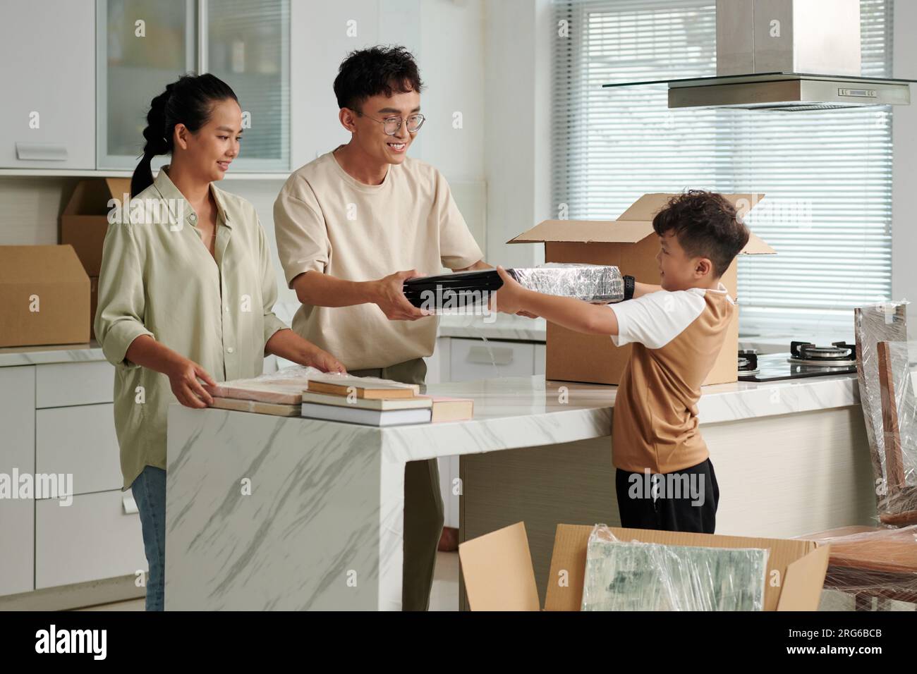 Cheerful parents asking son to put wrapped pictures in cardboard boxes ...