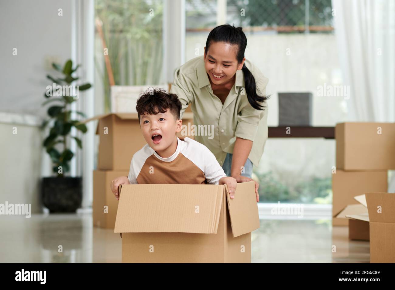 Mother pushing cardboard box with her son sitting inside Stock Photo ...