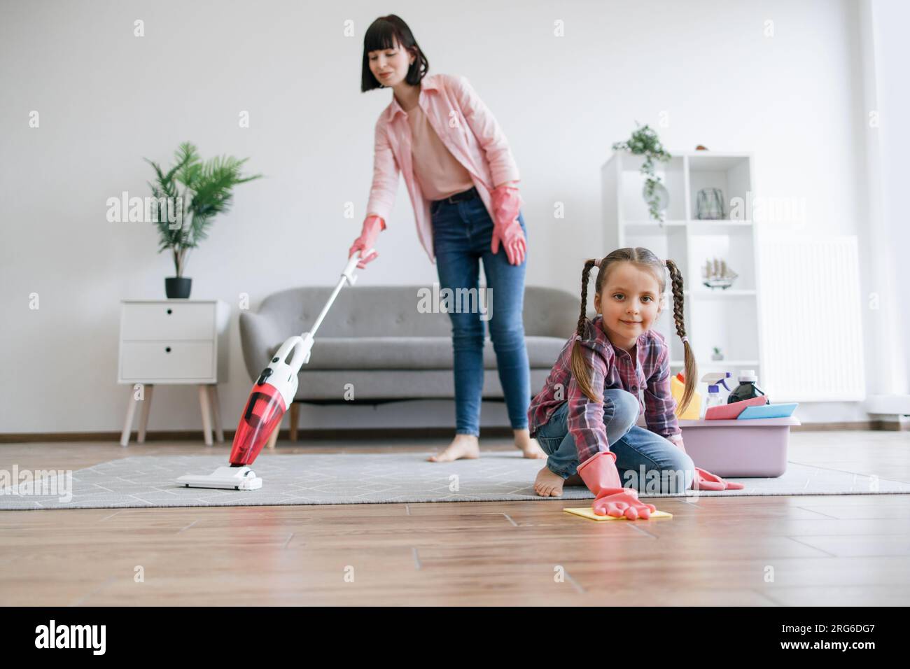 Preteen kid cleaning floor while mom hoovering room carpet Stock Photo ...