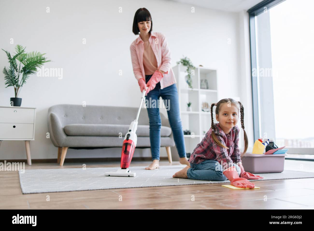 Preteen kid cleaning floor while mom hoovering room carpet Stock Photo ...