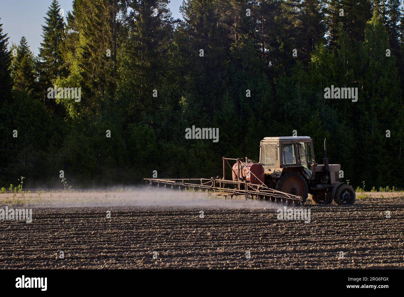 Mist cloud created by tractor mounted crop sprayer spreading herbicides ...