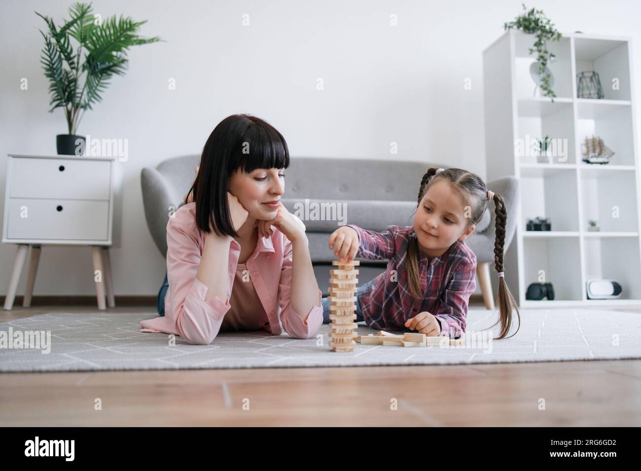 Child putting blocks in tumble tower while mom lying aside Stock Photo ...