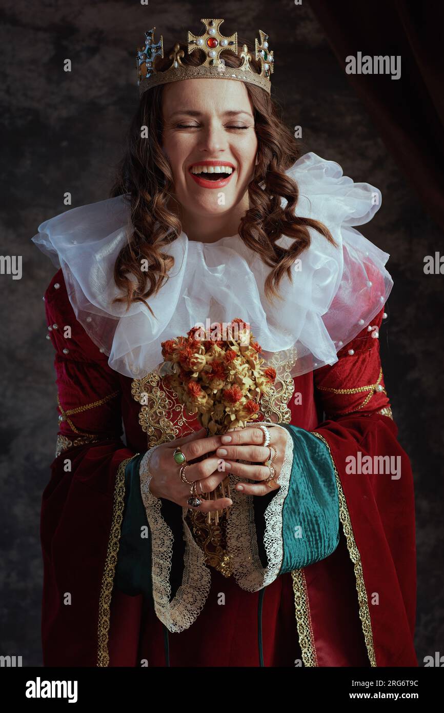 happy medieval queen in red dress with dried flower, white collar and ...